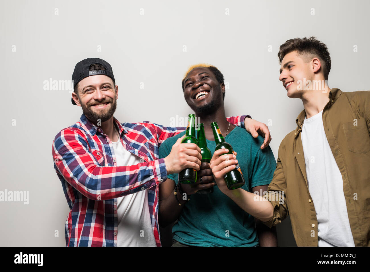 Three young joyful men holding beer and celebrating over gray ...