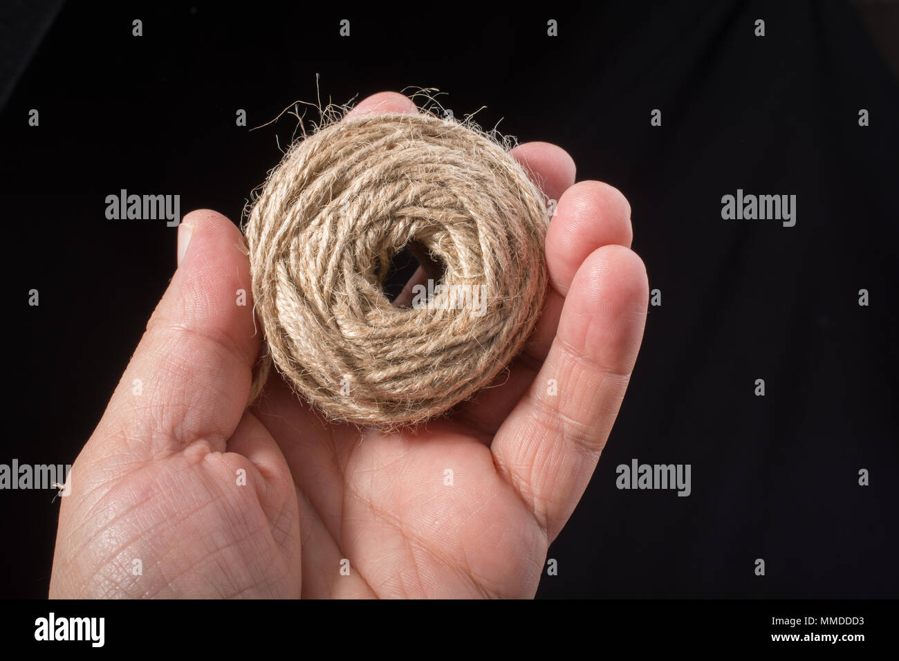 Spool of brown string in hand on black background Stock Photo - Alamy
