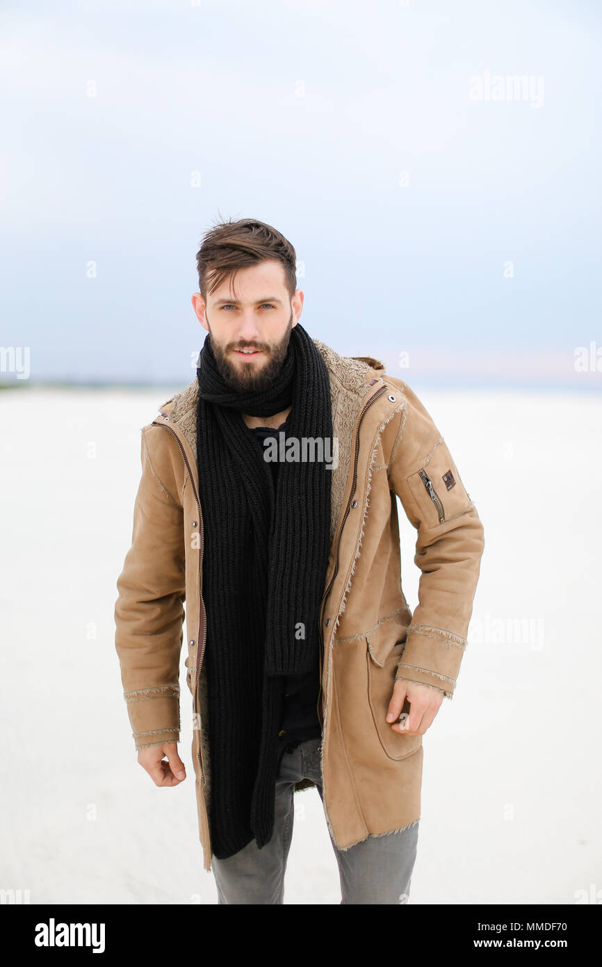 European young man with beard wearing coat and scarf standing in white ...