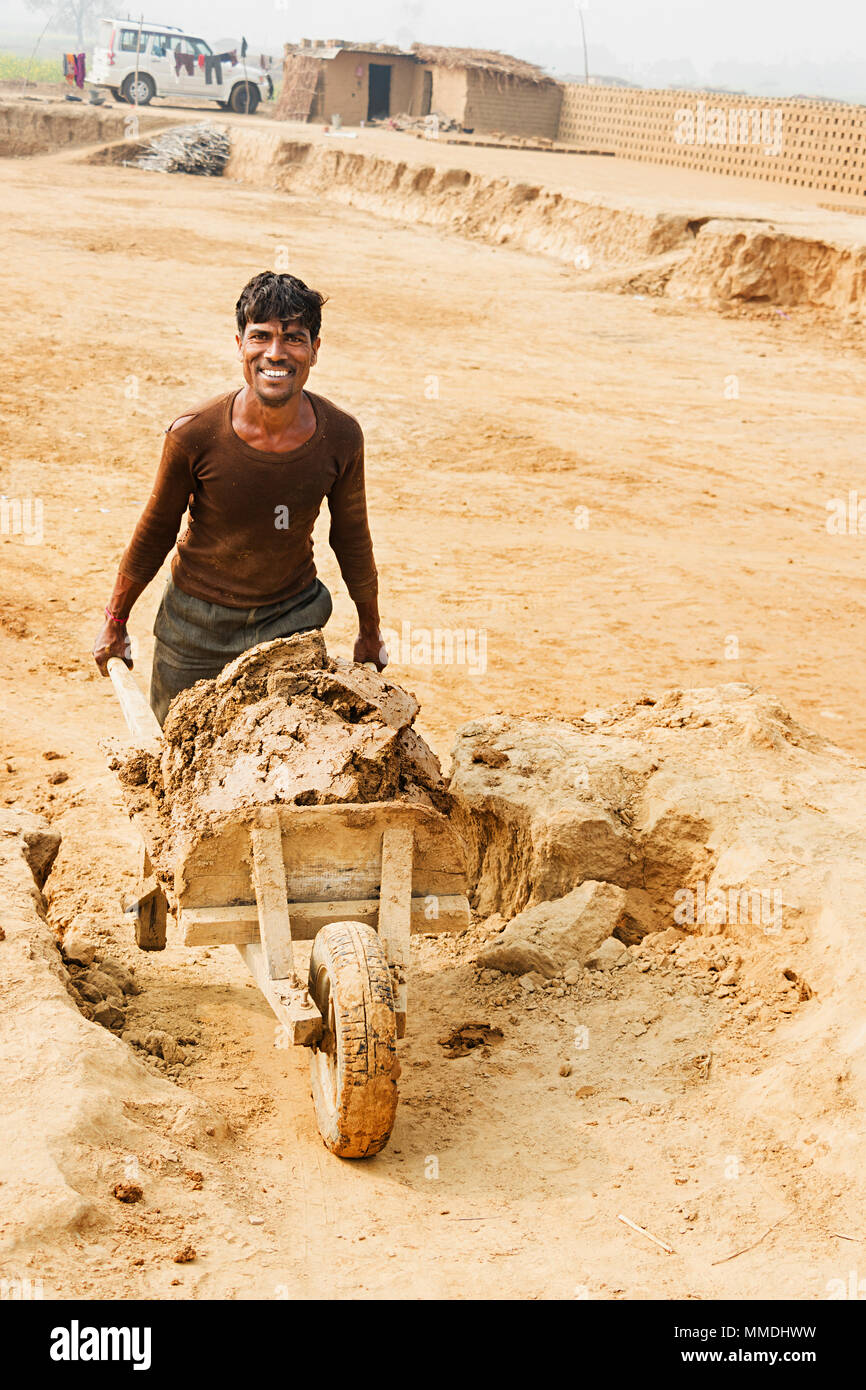 Rural male Labour Pushes Wheelbarrel at brick-factory outside village ...
