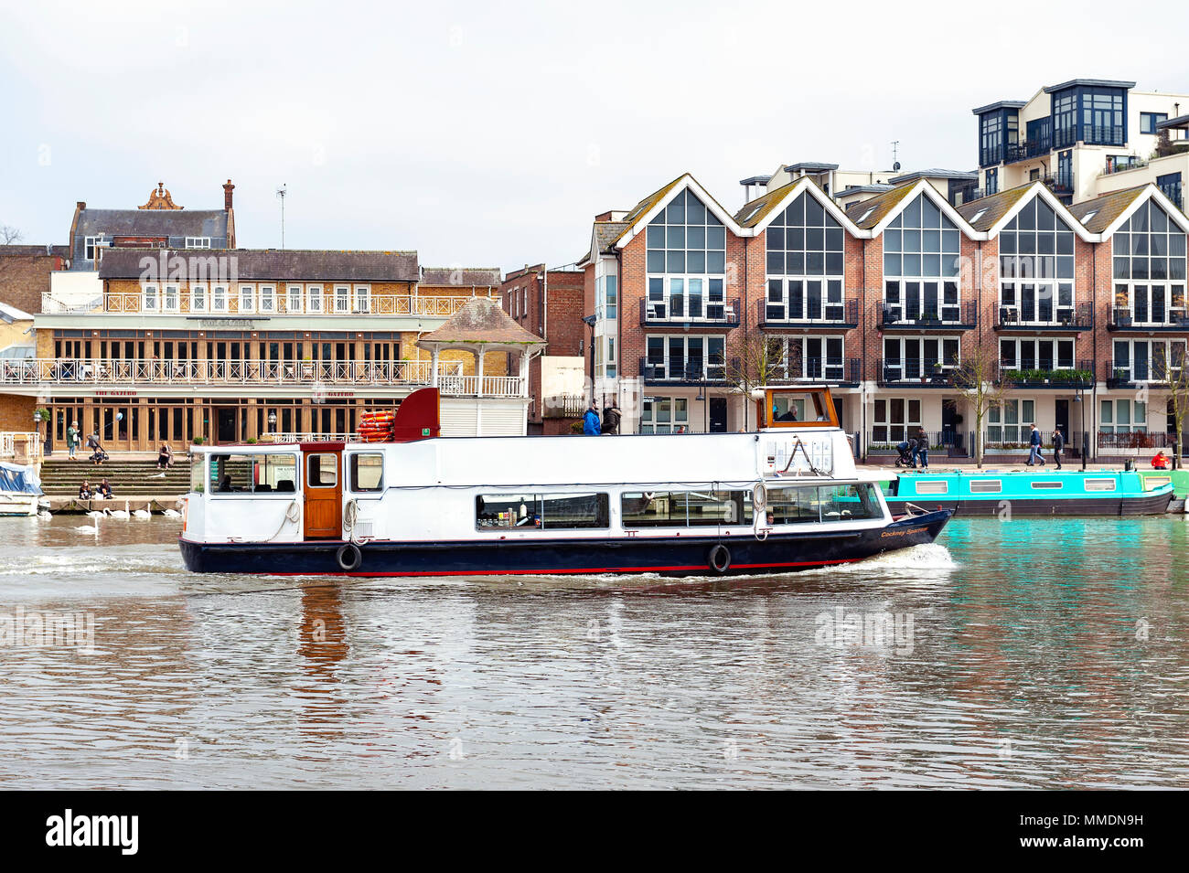 Tourist boat cruising along the River Thames passing the Riverside Walk ...