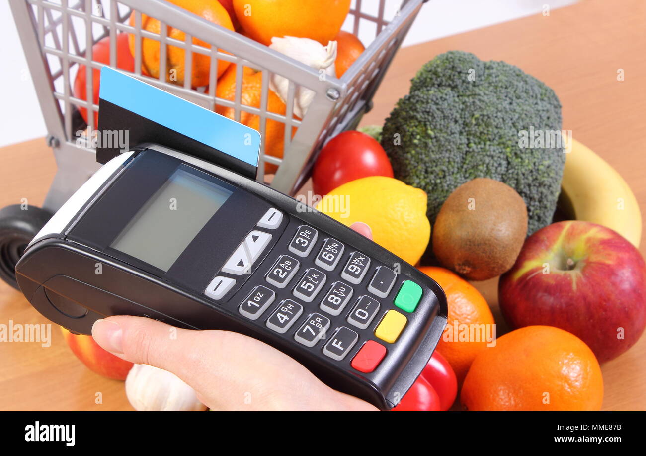 Hand using payment terminal with credit card and fruits and vegetables ...