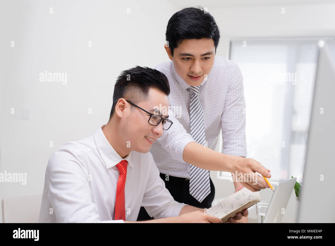 Two businessmen working together with computer at office desk, one of ...