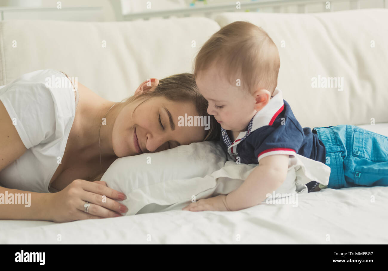 Toned image of 10 months old baby boy looking at mother sleeping in bed ...