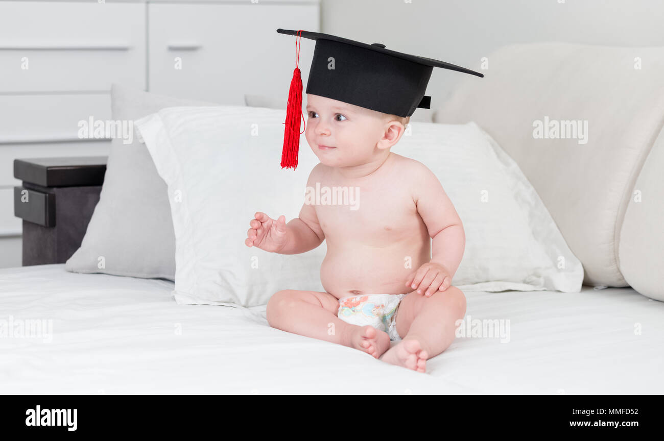 Cute 10 months old baby boy in dieapers wearing graduation cap with red ...