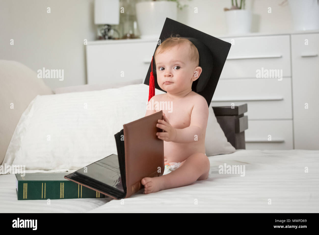 Cute baby in diapers wearing graduation cap turning pages of big book ...