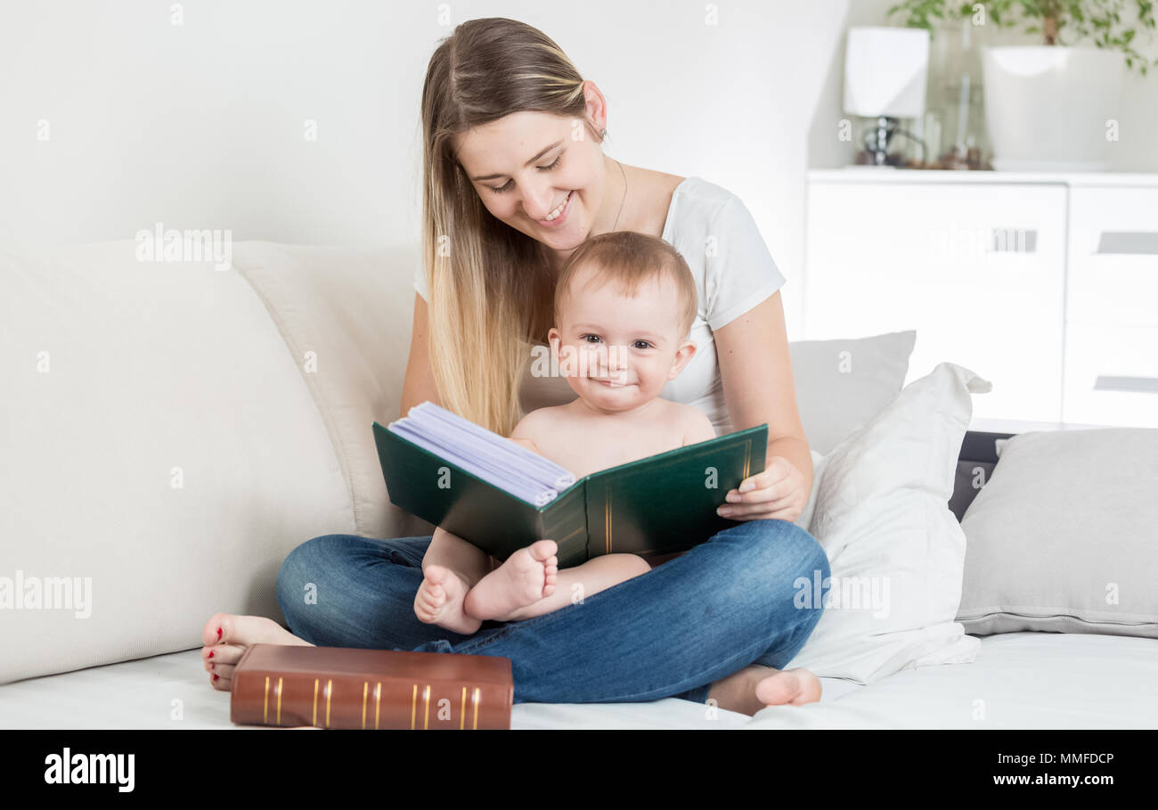 Happy smiling baby boy reading big old book on bed with mother Stock ...