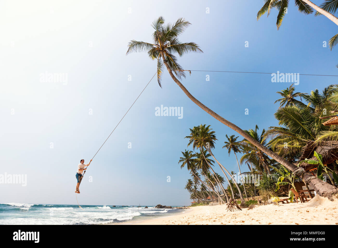 Young man having fun swinging on a rope at tropical island beach in Sri ...