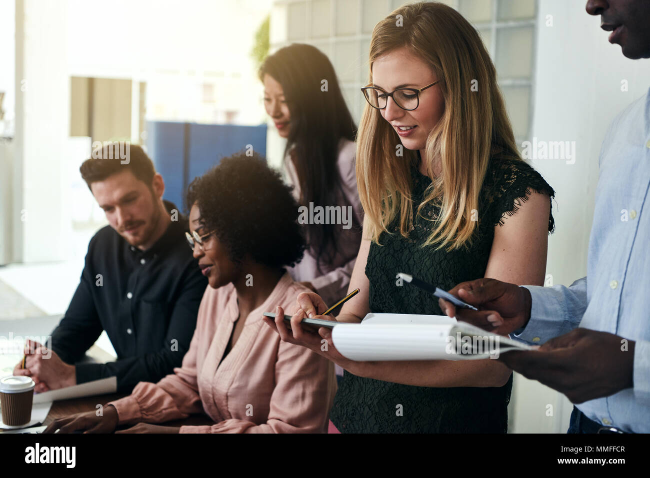 Two smiling coworkers comparing notes while standing in a modern office ...