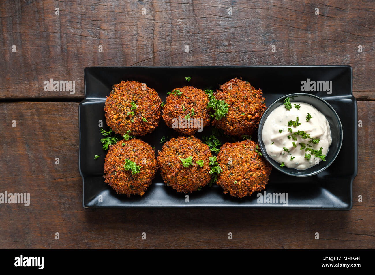 Fresh falafel with parsley and tzatziki sauce in black plate on wooden ...