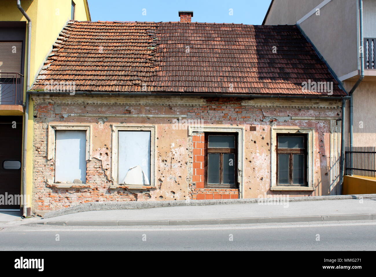 Small attached house damaged by shrapnels during war with falling facade, damaged roof tiles ...