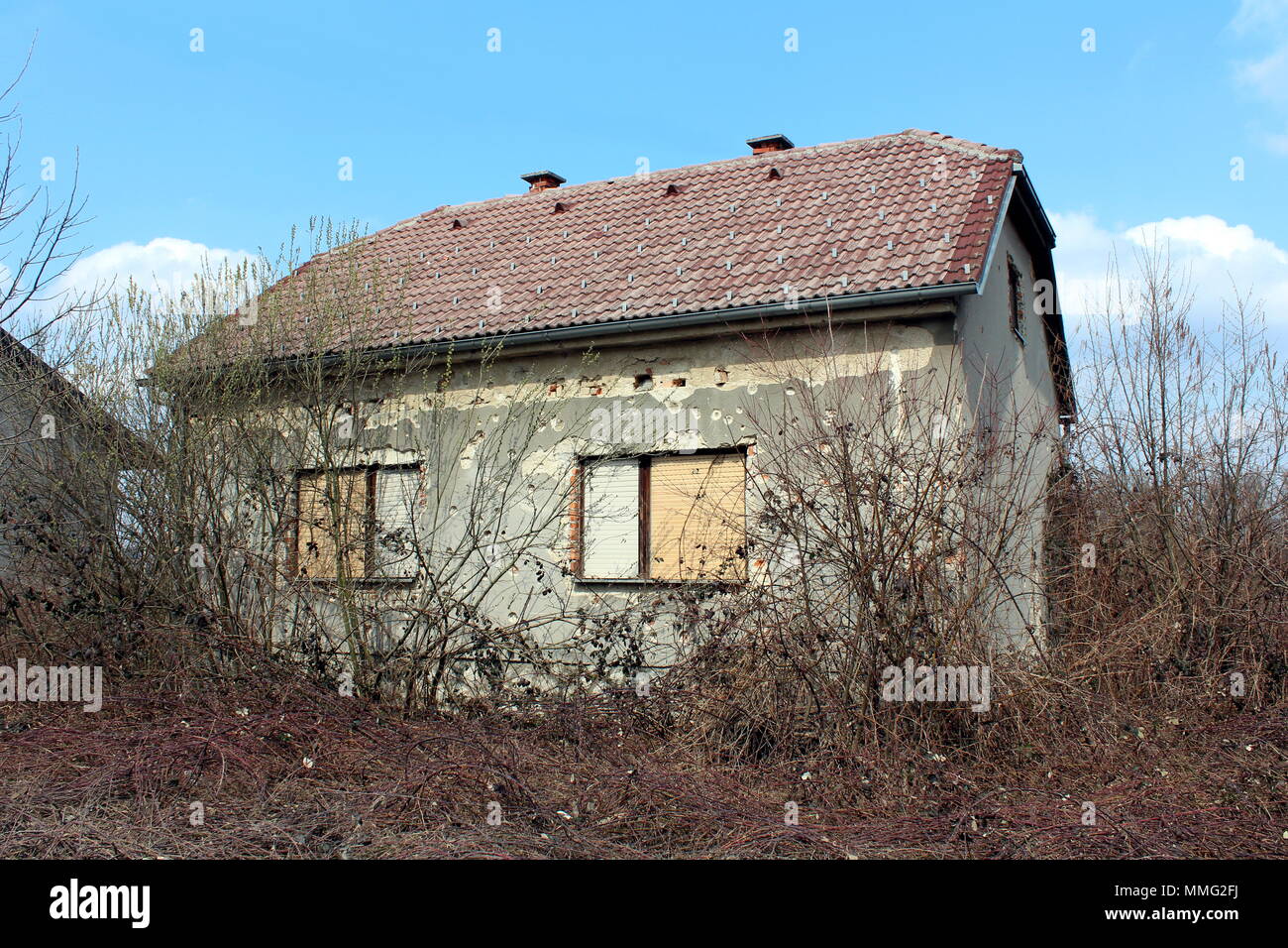 Small suburban family house damaged by shrapnels during war with dilapidated facade, visible ...