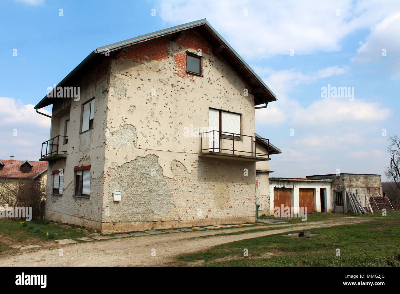 Suburban family house heavily damaged by shrapnels during war with dilapidated facade, rusted ...