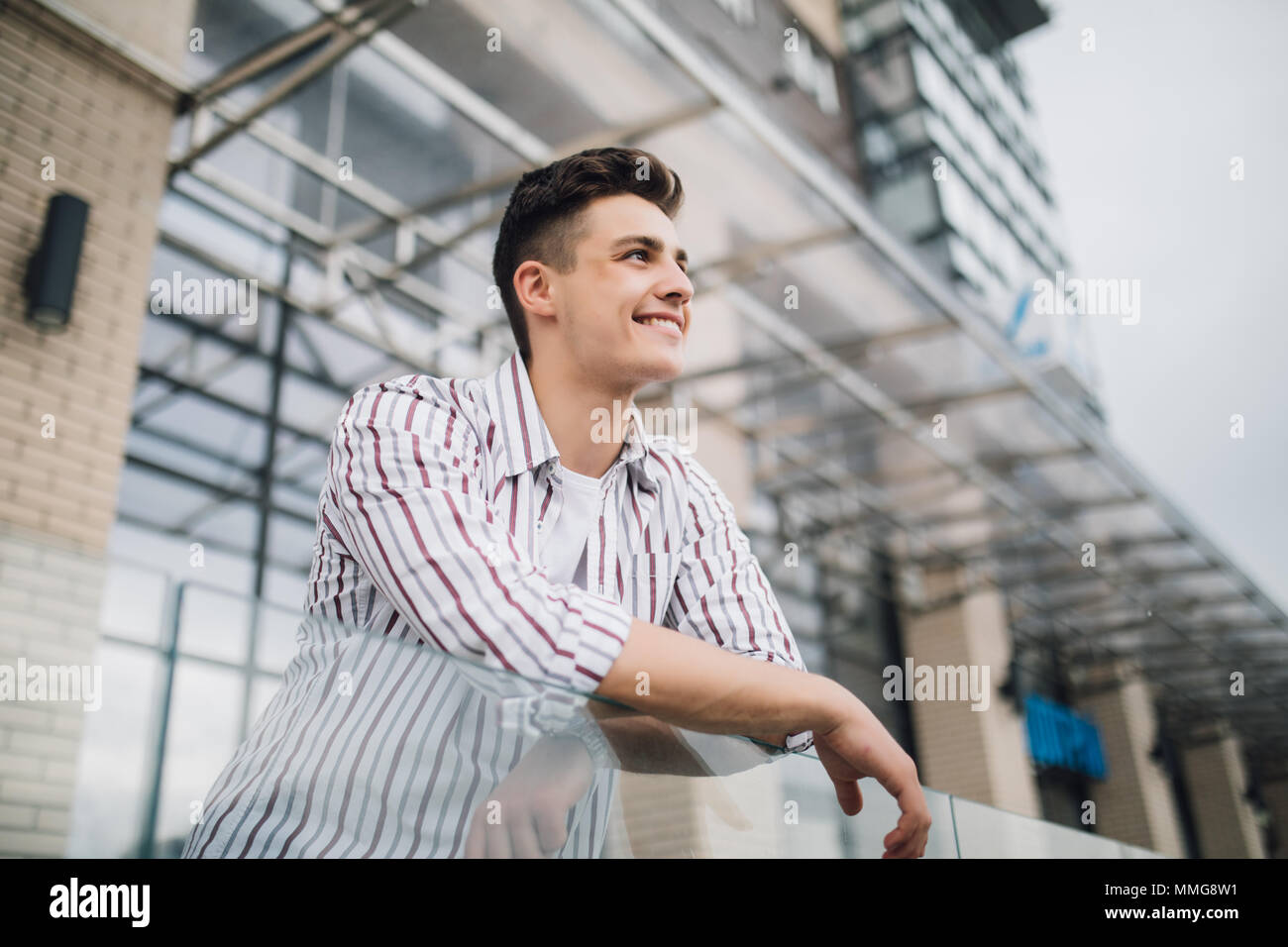 Joyful man enjoying life in city on balcony in front of modern building ...