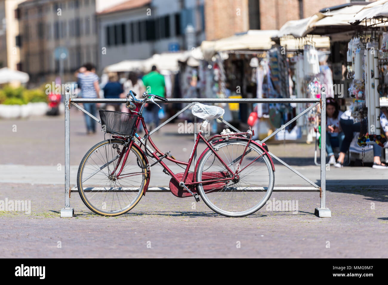 Red bicycle with basket chained to railing by street market in Padova ...