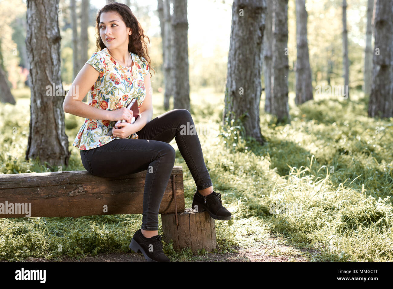 happy young girl sitting on a log in the forest, bright sunlight around ...