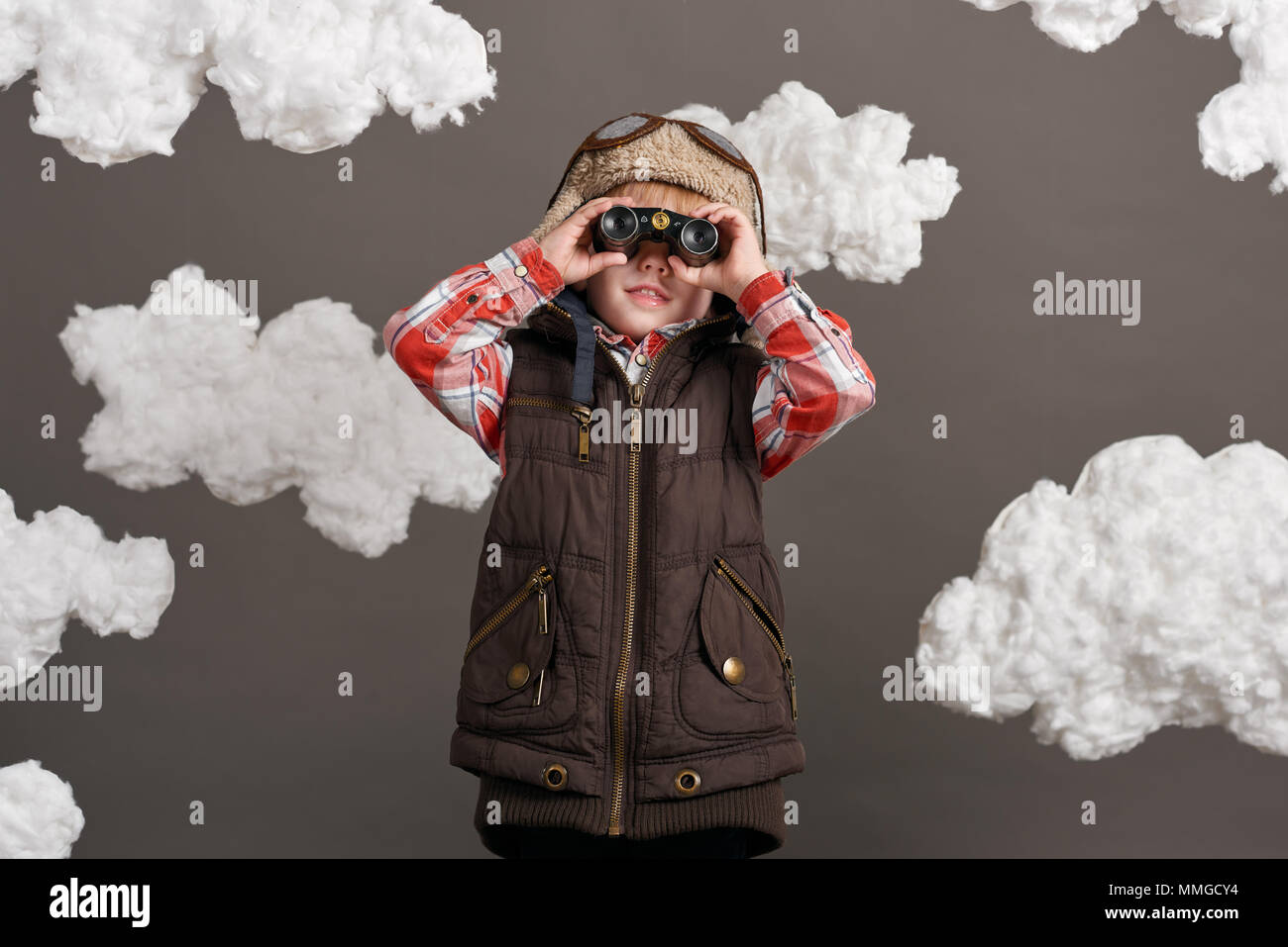 boy dressed as an airplane pilot stands between the clouds and looks ...