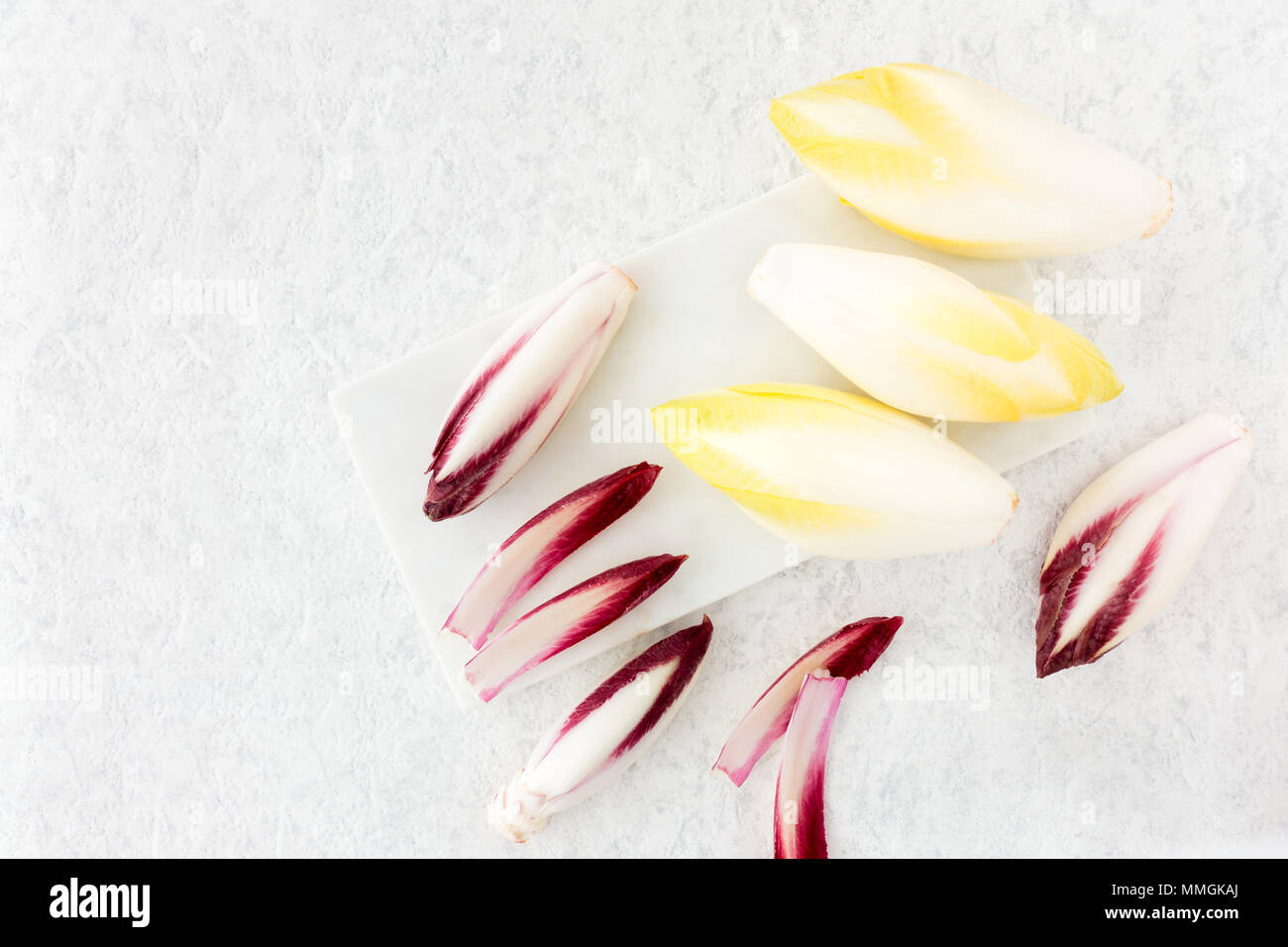 Whole chicory and red chicory leaves on a white marble chopping board ...
