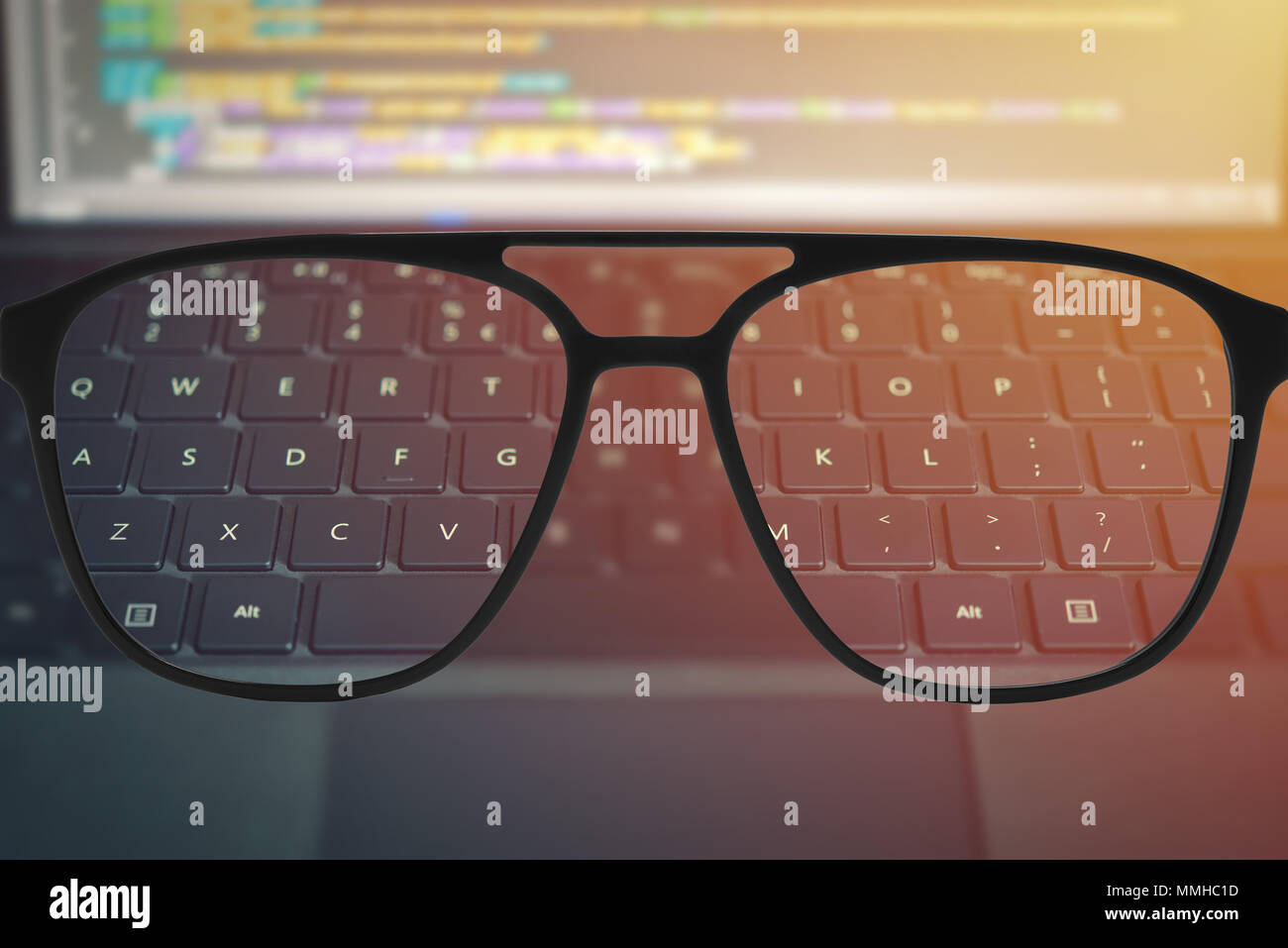 Clear image in glasses against blurry llaptop keyboard with code text ...