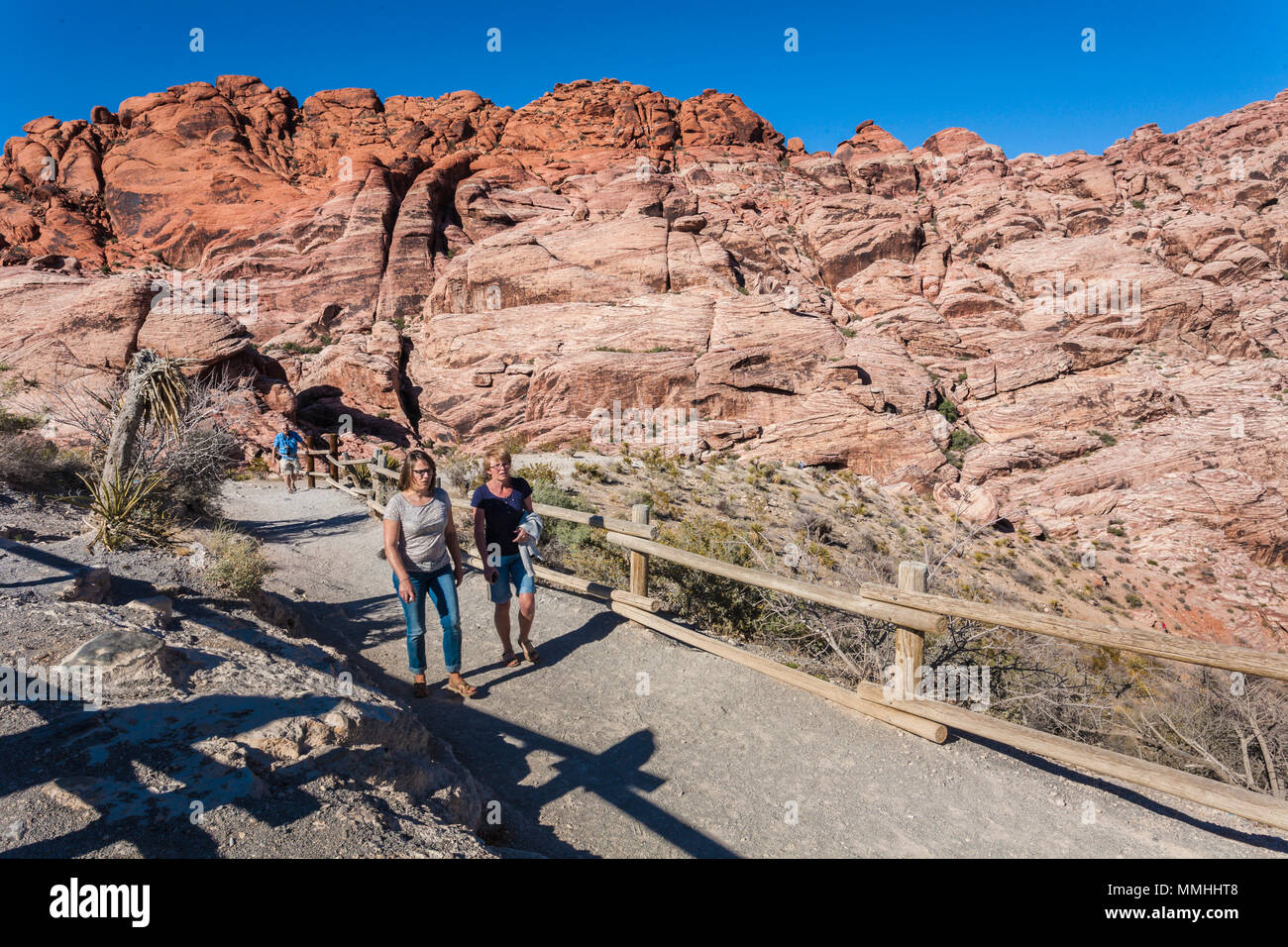 Park visitors walking past rock formations on a trail in Red Rock ...