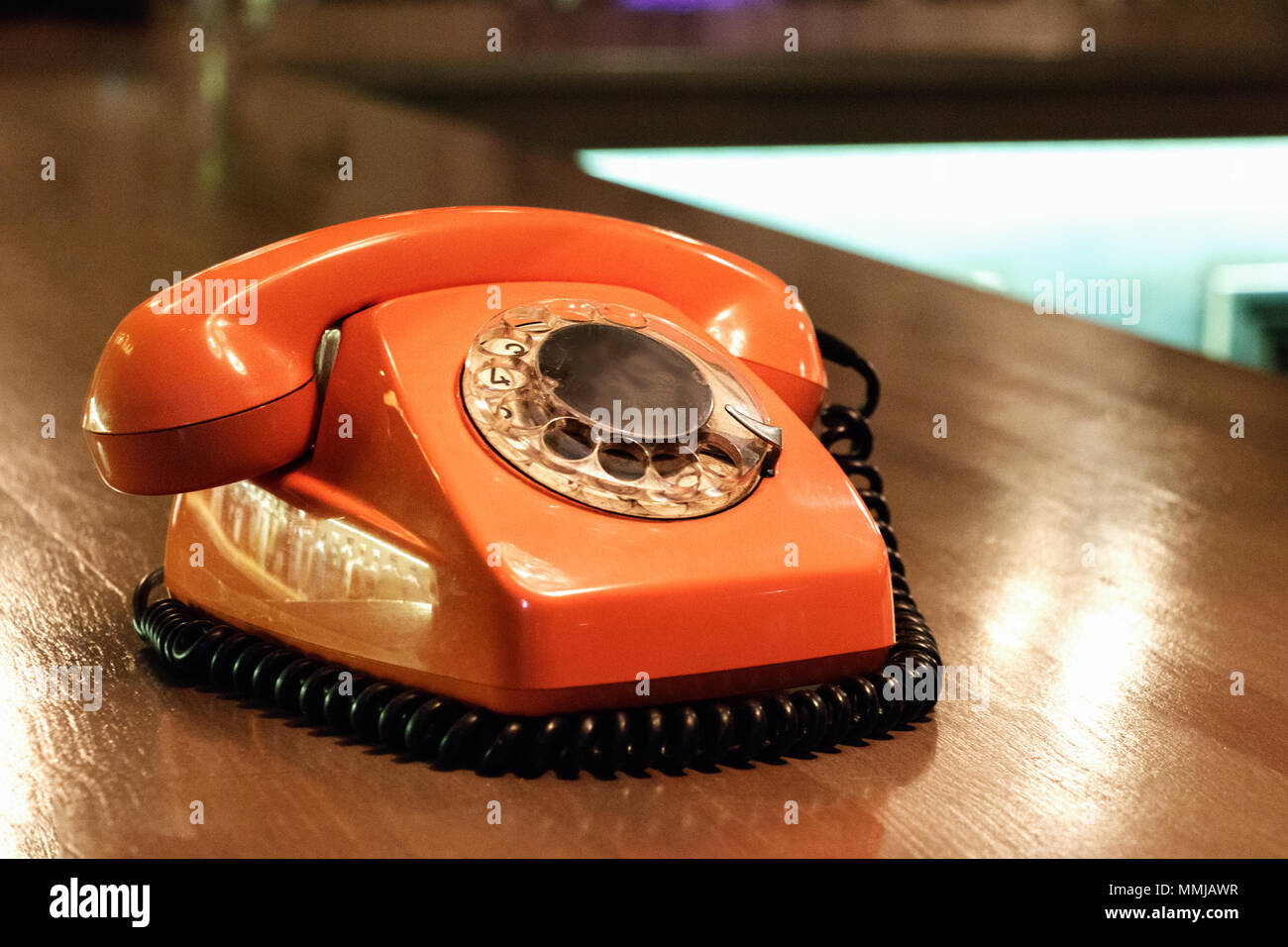 A vintage plastic orange telephone with dial placed on a wooden table ...