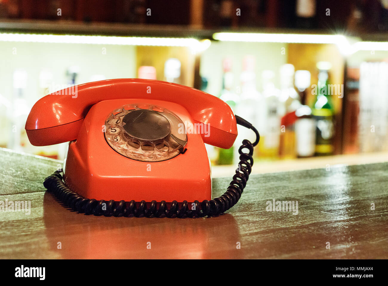 A vintage plastic orange telephone with dial placed on a wooden table ...
