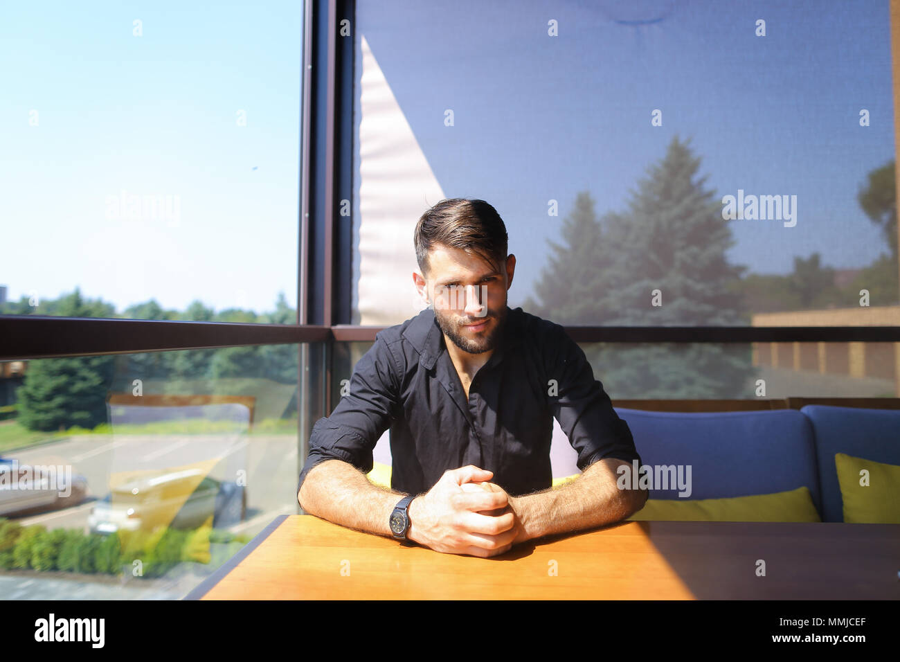European male manager sitting at office on sofa and wearing black shirt ...