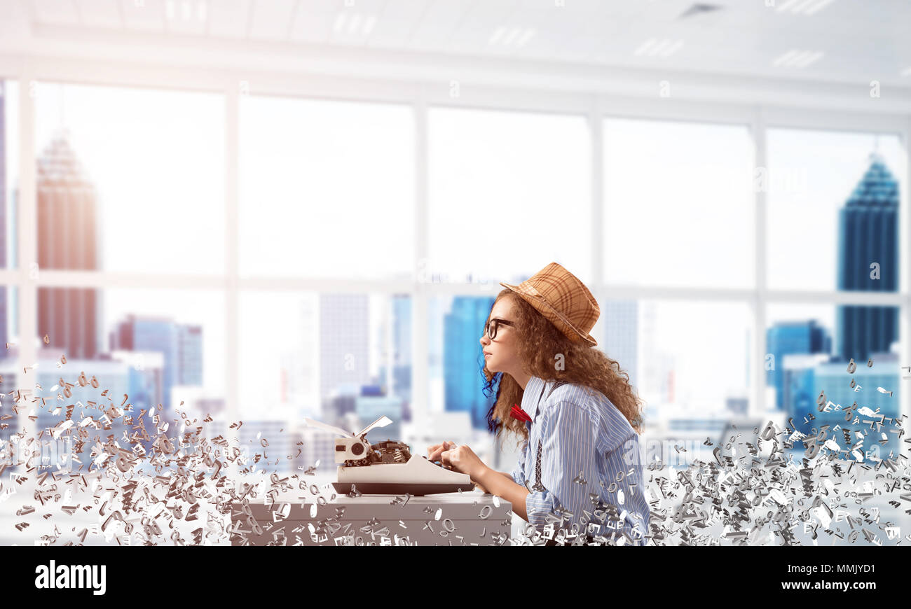 Young woman writer in hat and eyeglasses using typing machine while ...