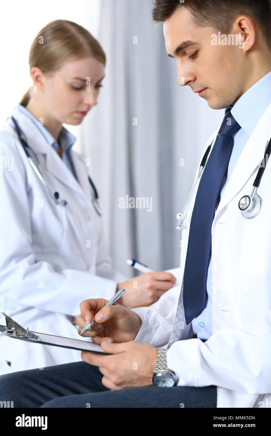 Doctors writing papers using clipboard. Physicians discussing ...