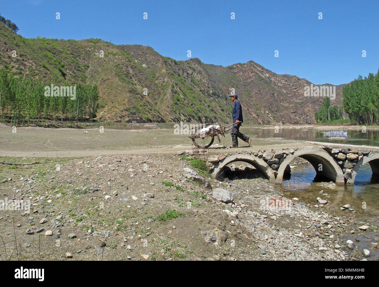 man pushing hand cart over bridge in stony valley Hebei, China May ...