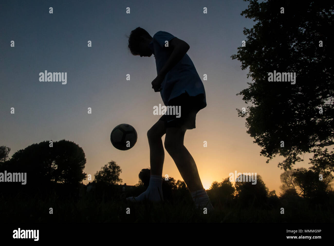 A boy practices his football skills as the sun goes down, playing ...