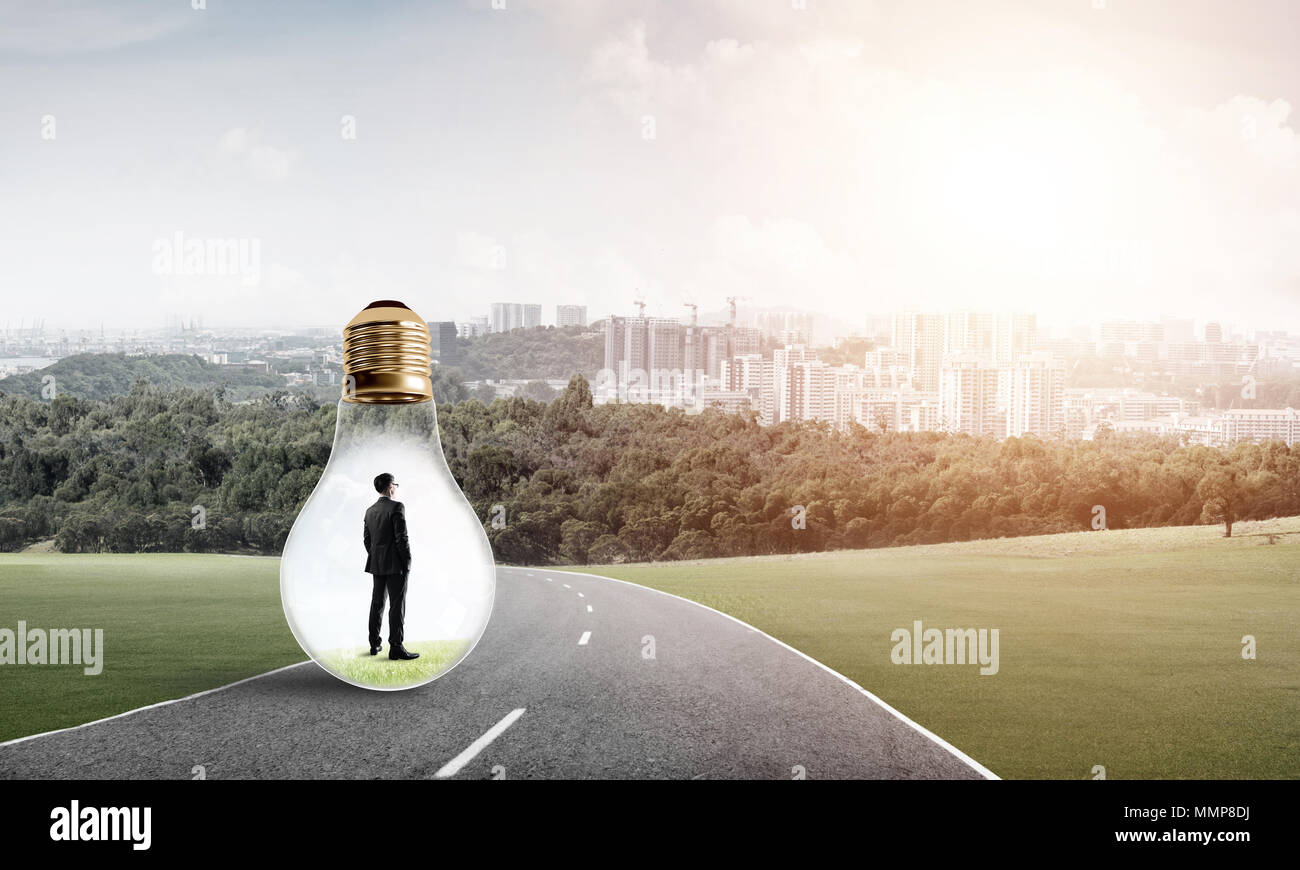 Young businessman trapped inside of light bulb on asphalt road Stock ...