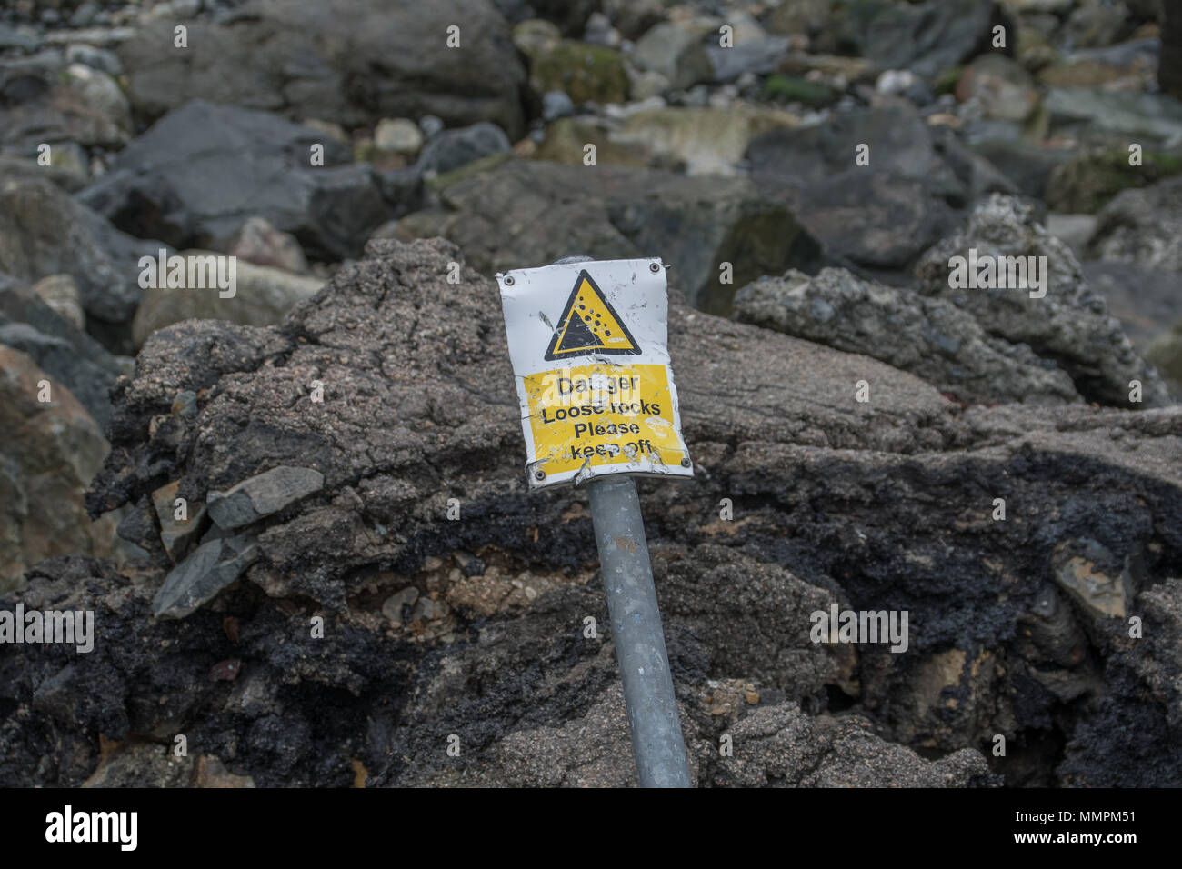 Danger loose rocks sign which has been bent and is falling over against ...