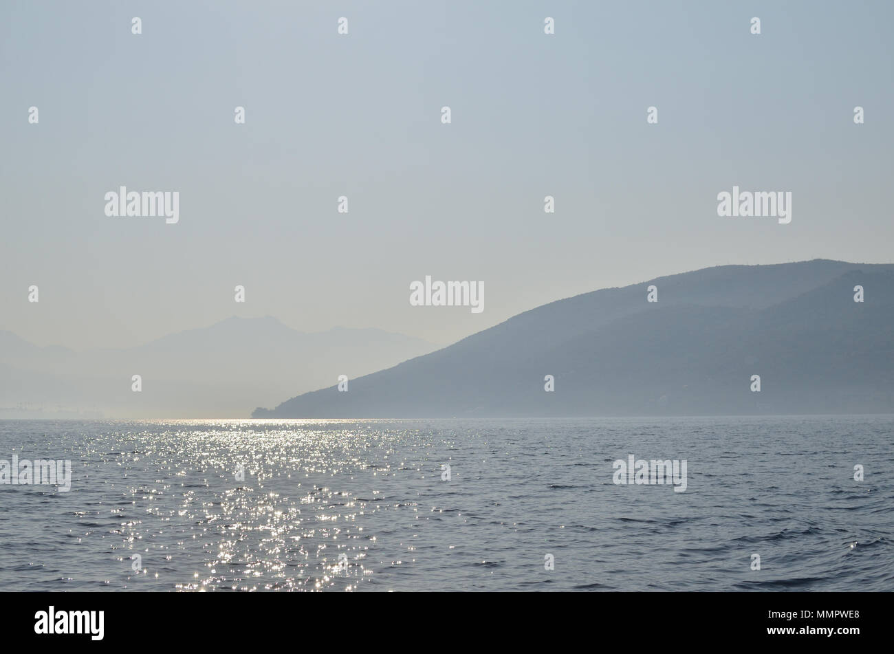 Calm sea surface with a land in a distance with a morning mist and ...