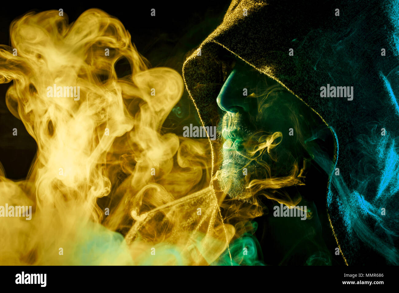 A young man in a black cape smokes and exhales large clouds of colored ...