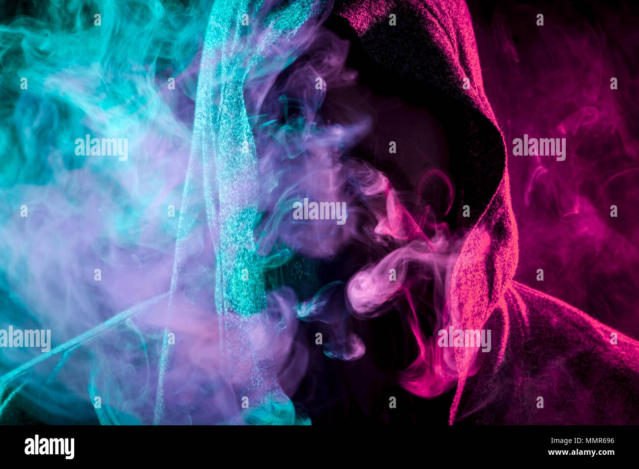 A young man in a black cape smokes and exhales large clouds of colored ...