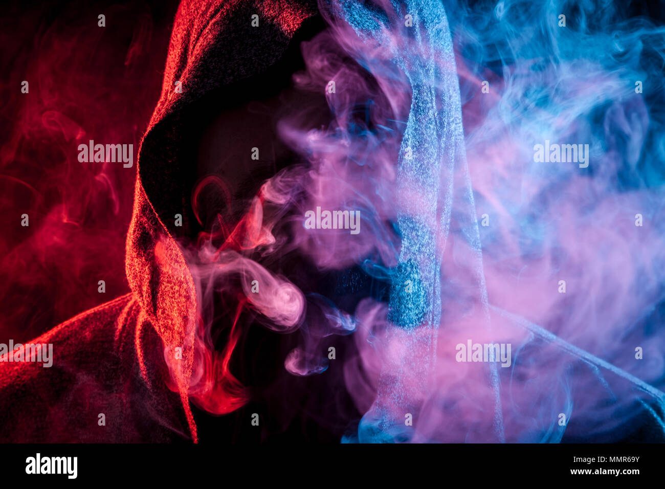 A young man in a black cape smokes and exhales large clouds of ...