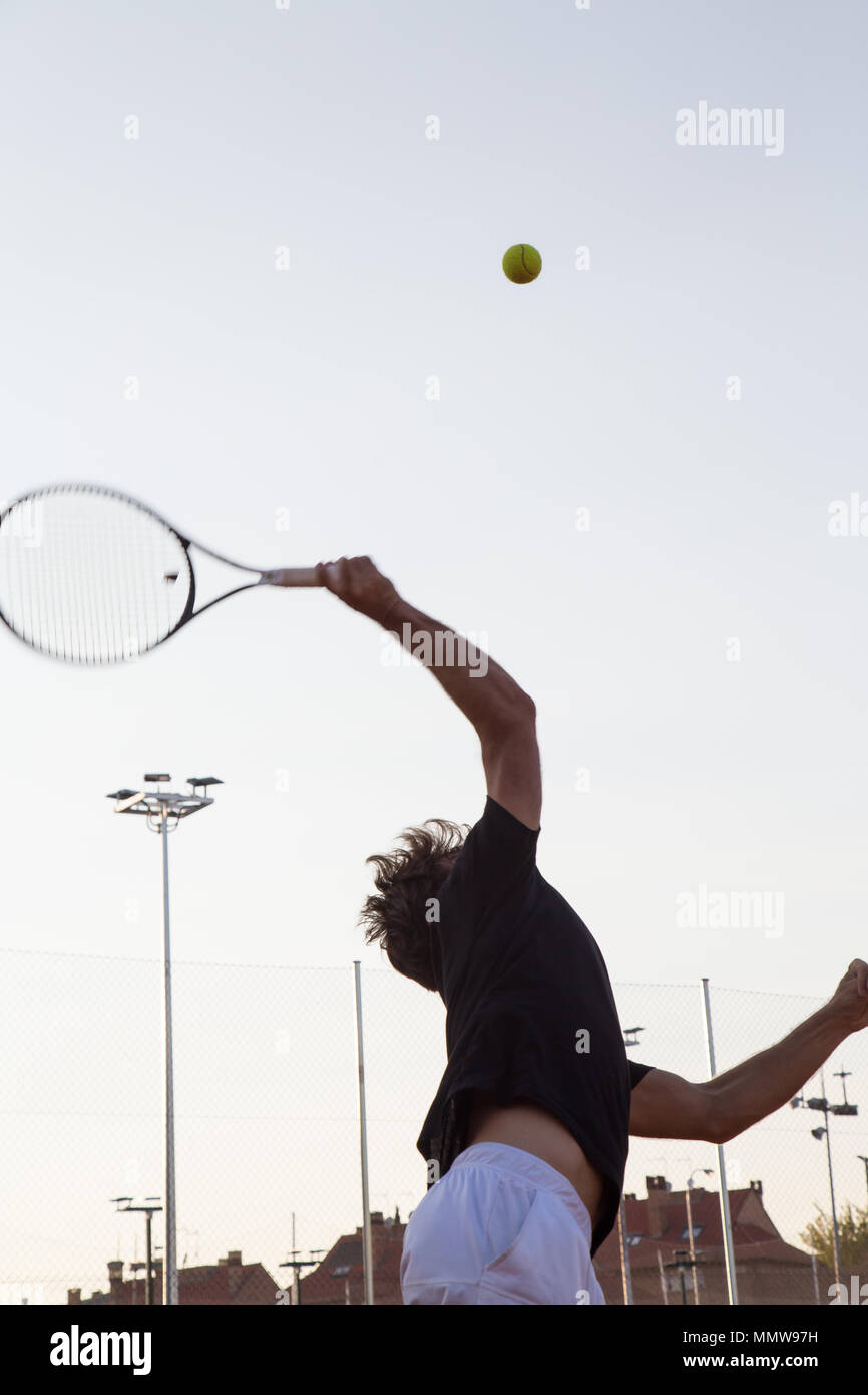 Back view of sportsman with tennis racket hitting ball in back light on ...