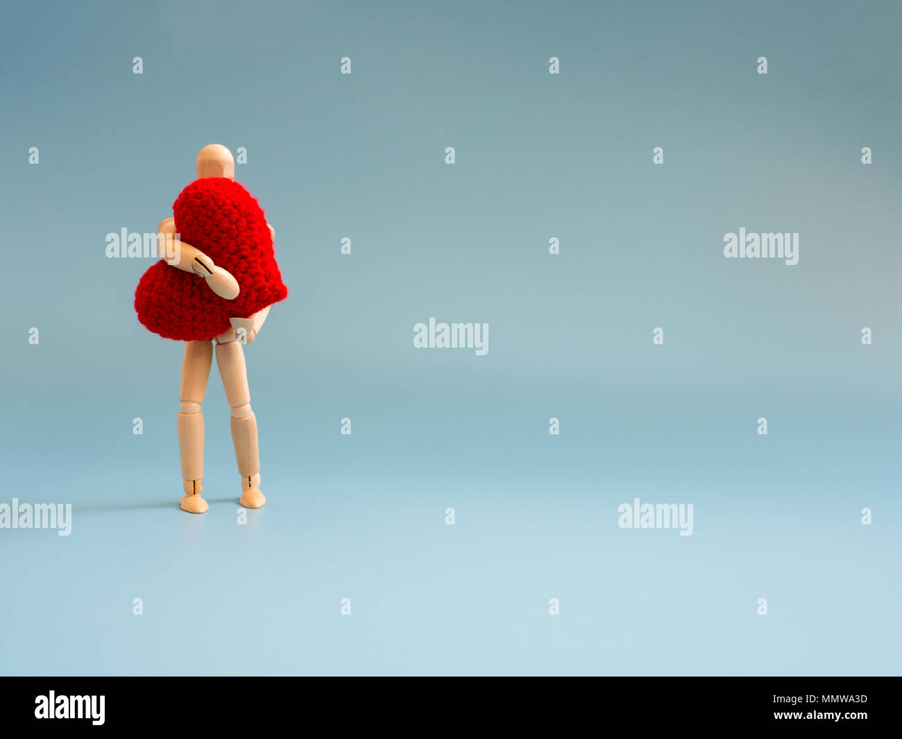 Wooden puppet standing and holding a red heart on the blue screen ...