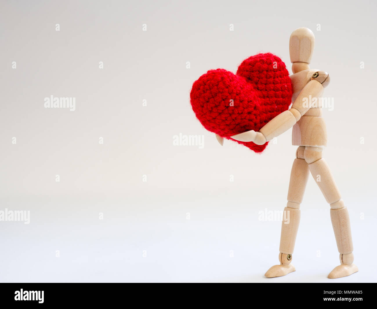 Wooden puppet standing and holding a red heart on the white screen ...