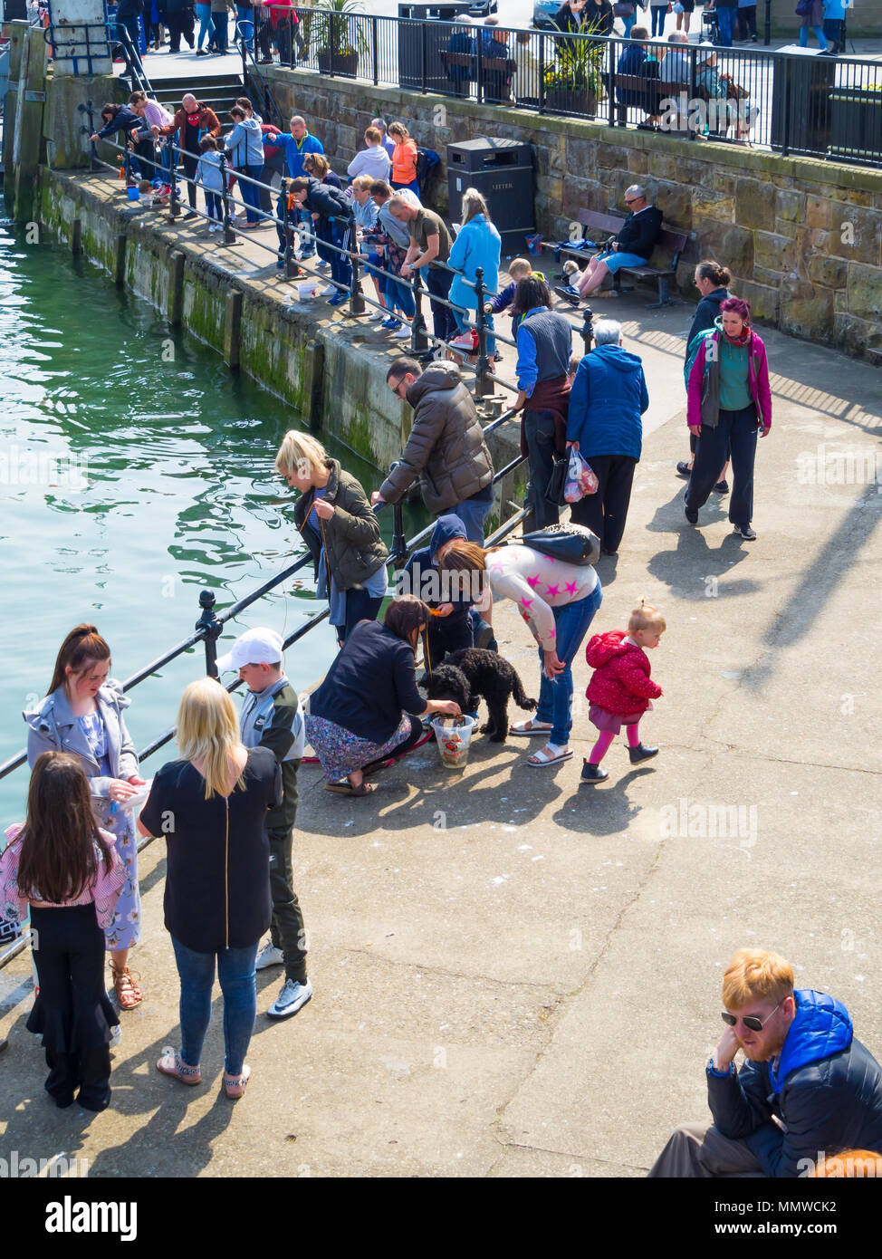 A crowd of holidaymakers in spring sunshine fishing by the bridge in ...