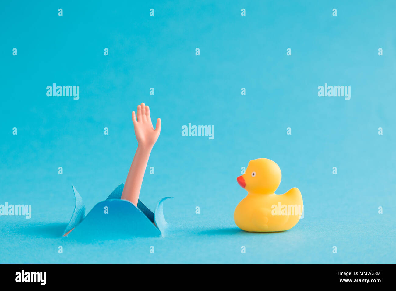 Doll arm emerging from blue paper background and yellow rubber duck ...