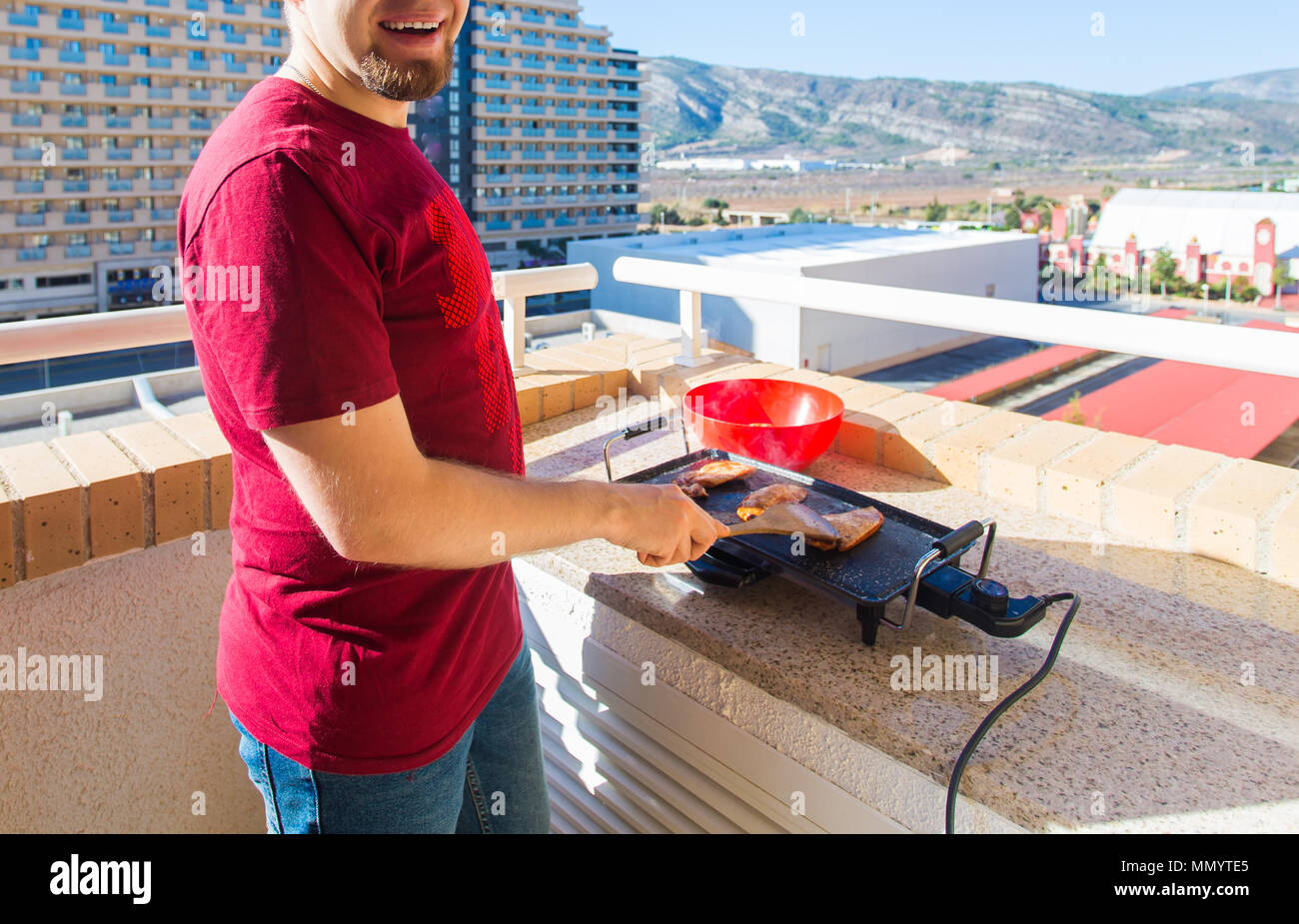 Young man grilling chicken on the balcony Stock Photo - Alamy