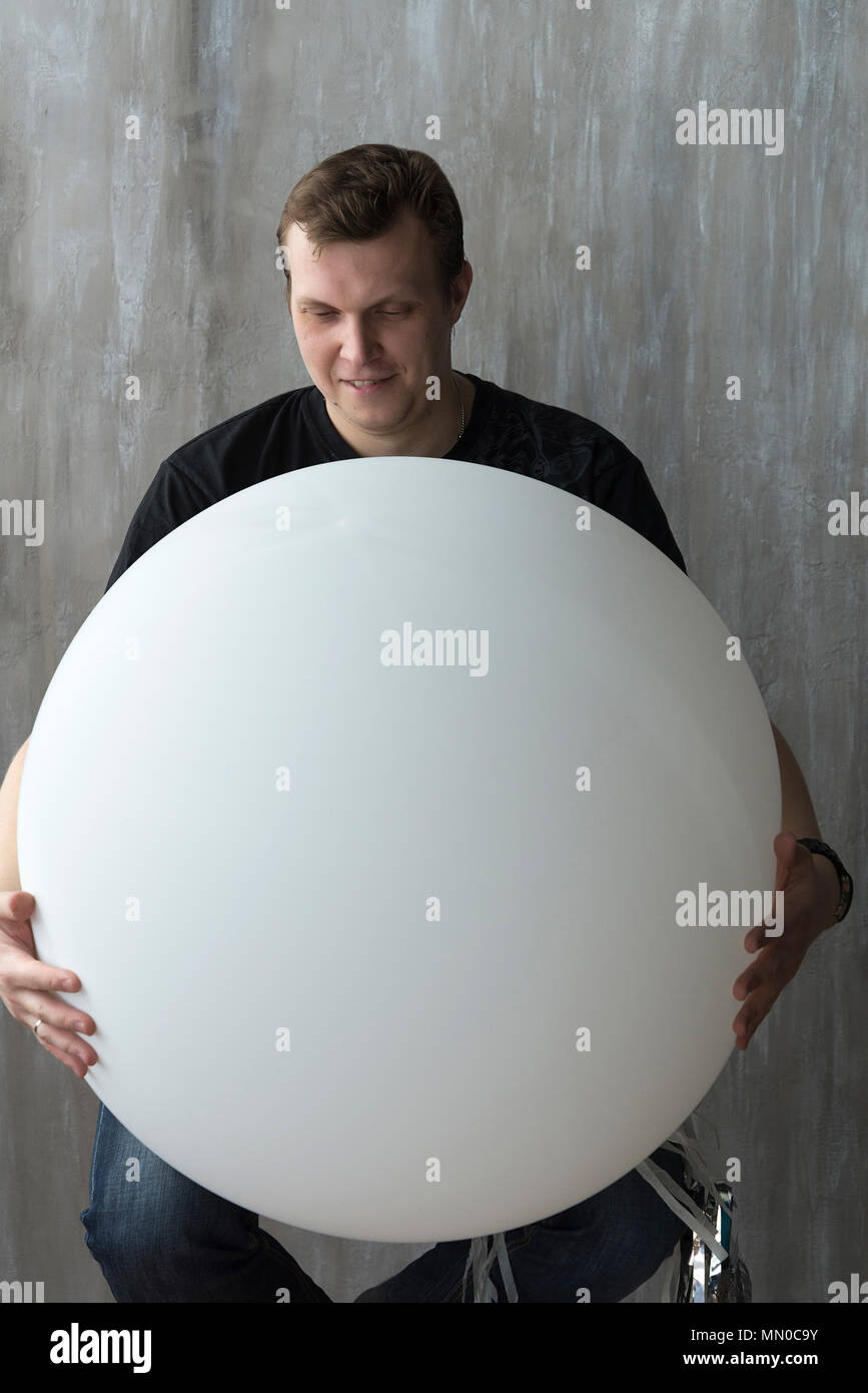 A man holding an inflatable ball on a gray background. Big ball, brutal ...