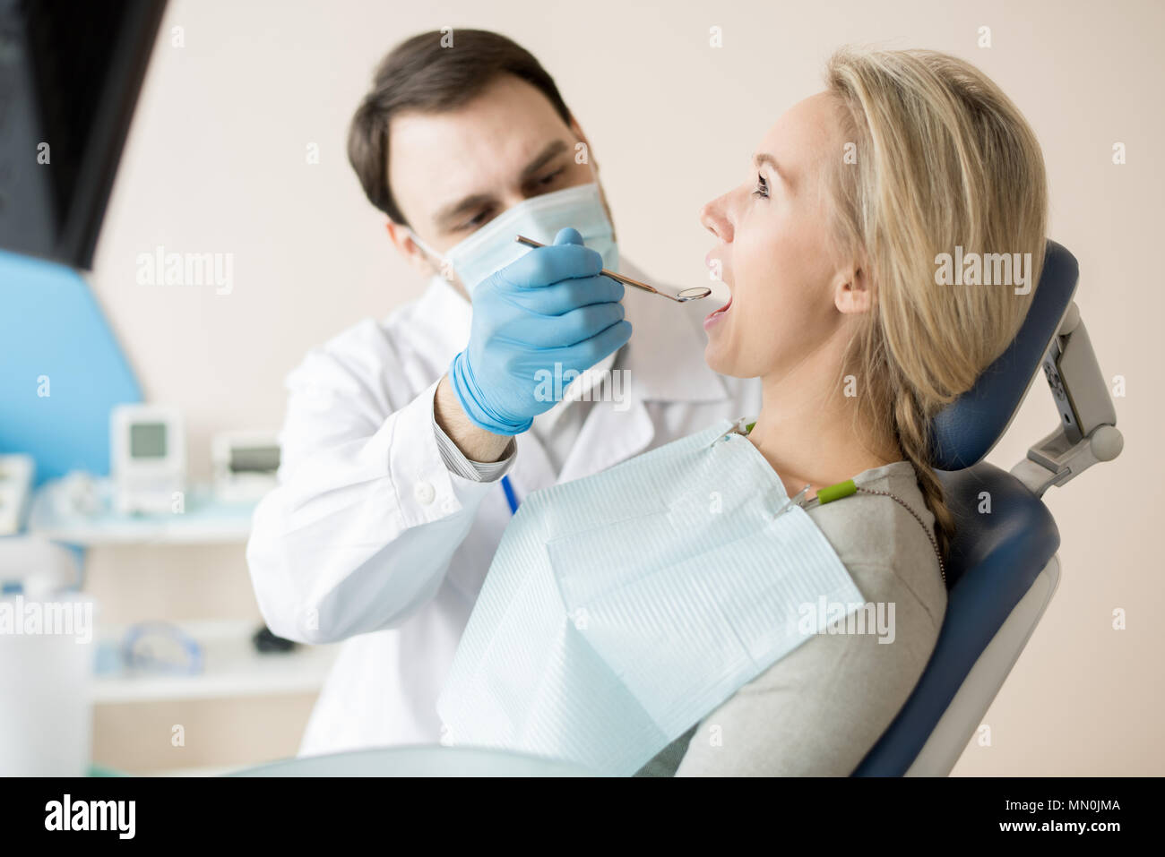 Side view of girl sitting in chair while dentist with small mirror ...