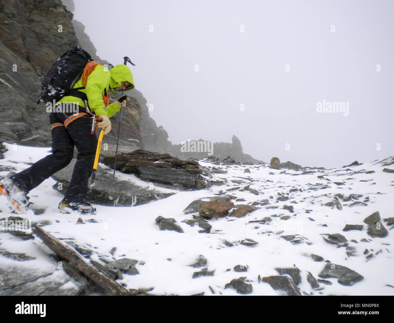 male mountain climber heading up a steep snow and rock slope in bad ...