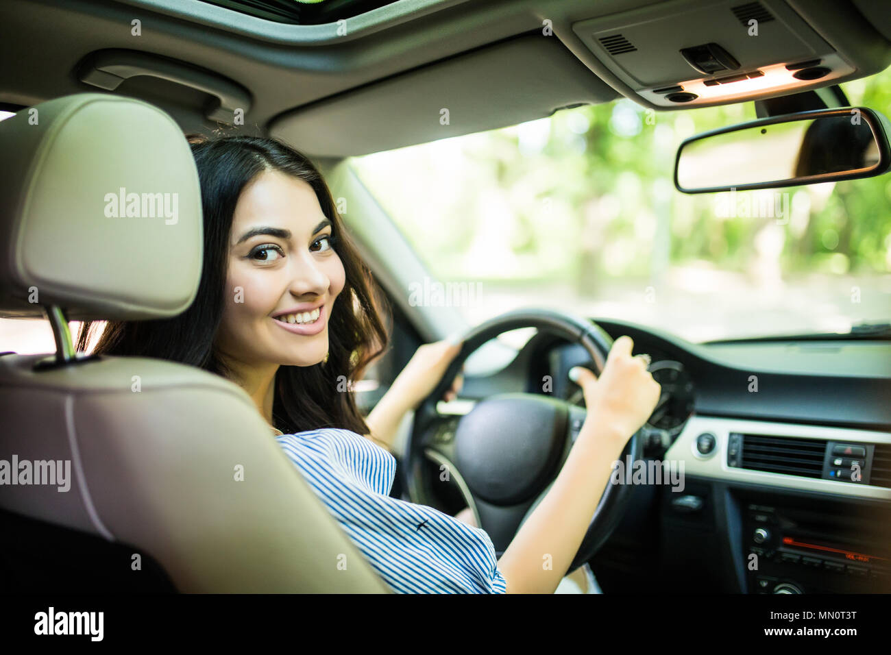 Woman driver looking over the back of the drivers seat into the rear of ...