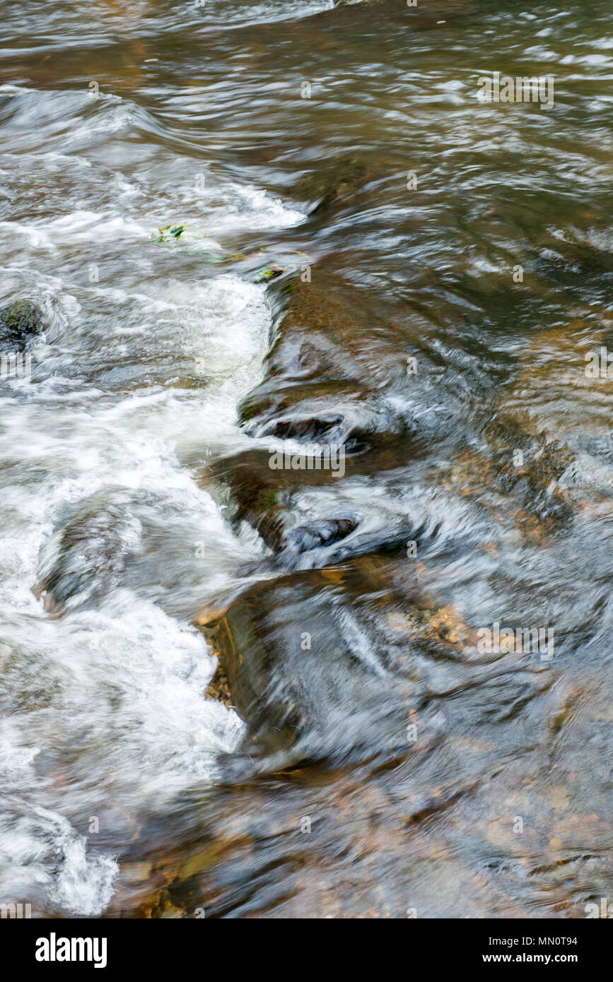 Water in a river flowing over rocks in a small waterfall, calm on one ...