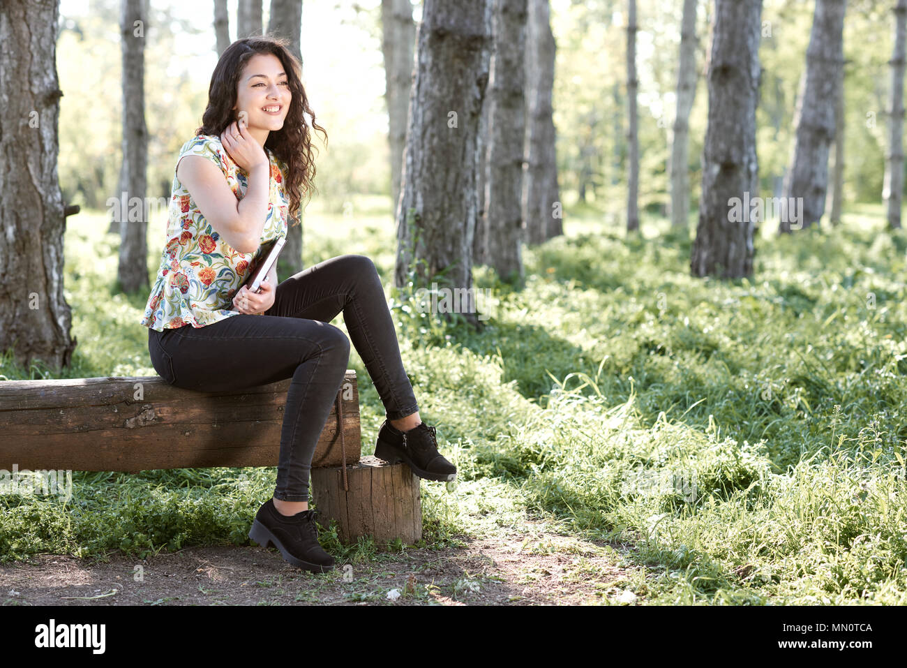 happy young girl sitting on a log in the forest, bright sunlight around ...