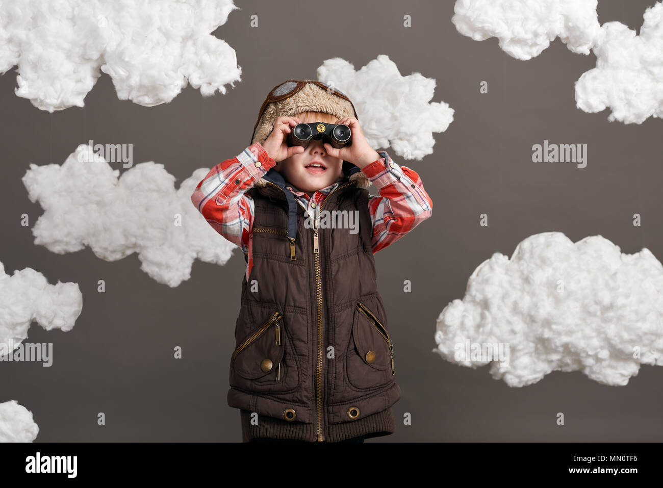 boy dressed as an airplane pilot stands between the clouds and looks ...